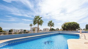 Piscina com águas azuis cristalinas, rodeada por palmeiras e vista para o horizonte urbano.