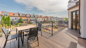 Um deck de madeira com uma mesa e cadeiras, guarda-corpo de metal e vista para casas vizinhas.