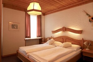 Uma cama de casal com cabeceira de madeira, mesa de cabeceira e luminária suspensa.