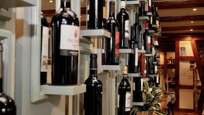 Uma estante para vinhos com várias garrafas, um vaso de planta e um balcão de madeira.