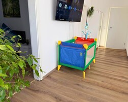 Um quarto com televisão na parede, um cercadinho e uma porta.