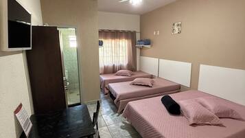 Quarto com duas camas, uma escrivaninha, uma cadeira, uma televisão e um ventilador de teto.