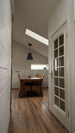 Uma área de refeições com mesa e cadeiras de madeira, uma luminária pendente, uma janela com vista e uma porta branca.