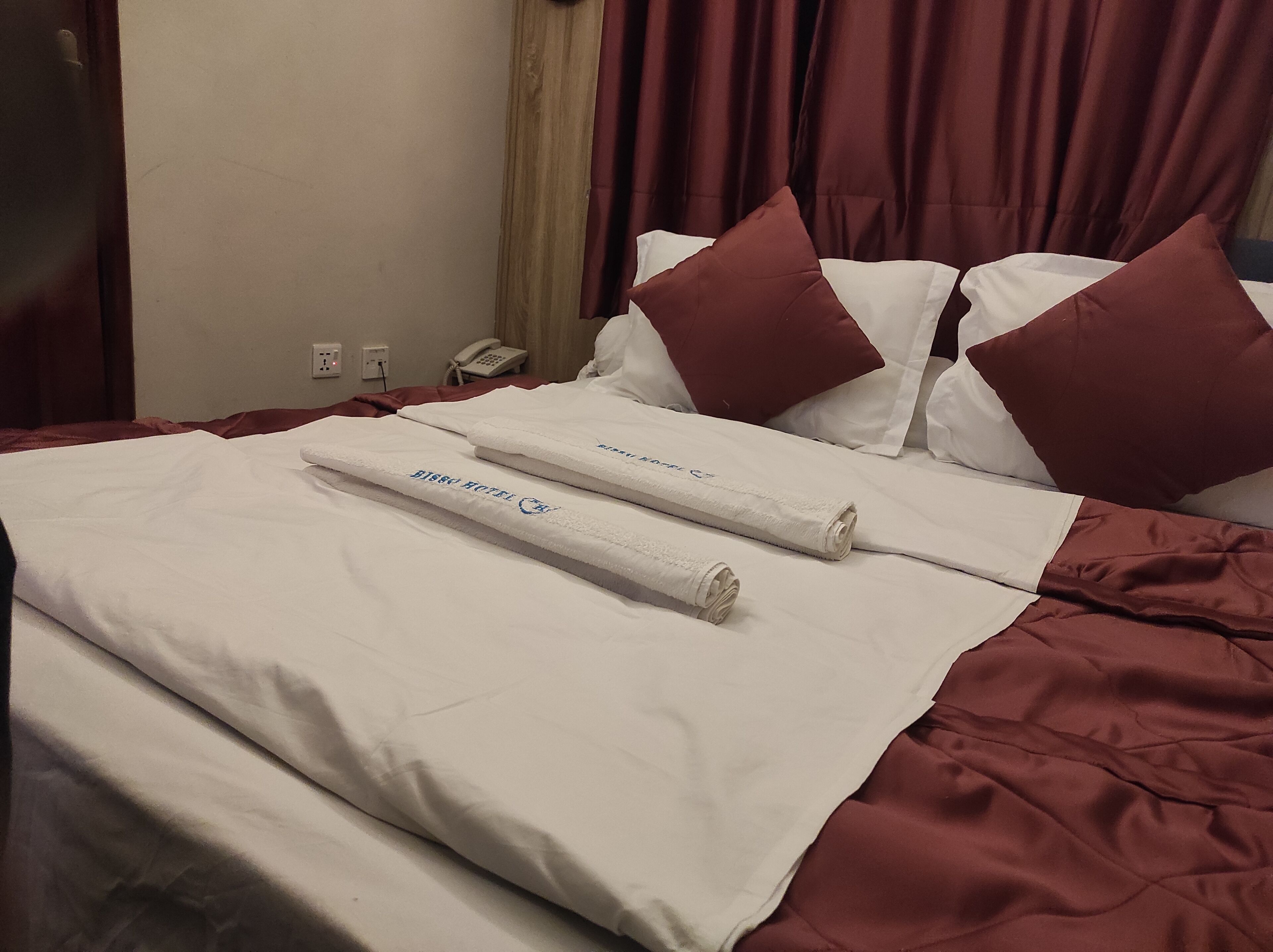 Quarto de hotel com cama, almofadas e toalha enrolada.