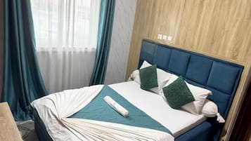 Cama bem arrumada com cabeceira azul, roupa de cama branca e um toque de cor verde-água.