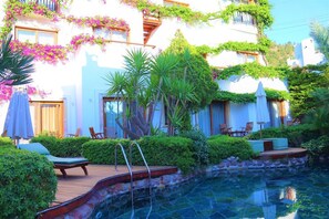 Uma área à beira da piscina com um deck de madeira, espreguiçadeiras e um muro de pedra.