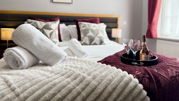 Quarto de hotel com cama bem arrumada, uma garrafa de vinho e copos em um jogo de chá.