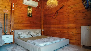 Quarto de cabana de madeira com uma cama, um criado-mudo, um aquecedor, um ar condicionado e um guarda-roupa.