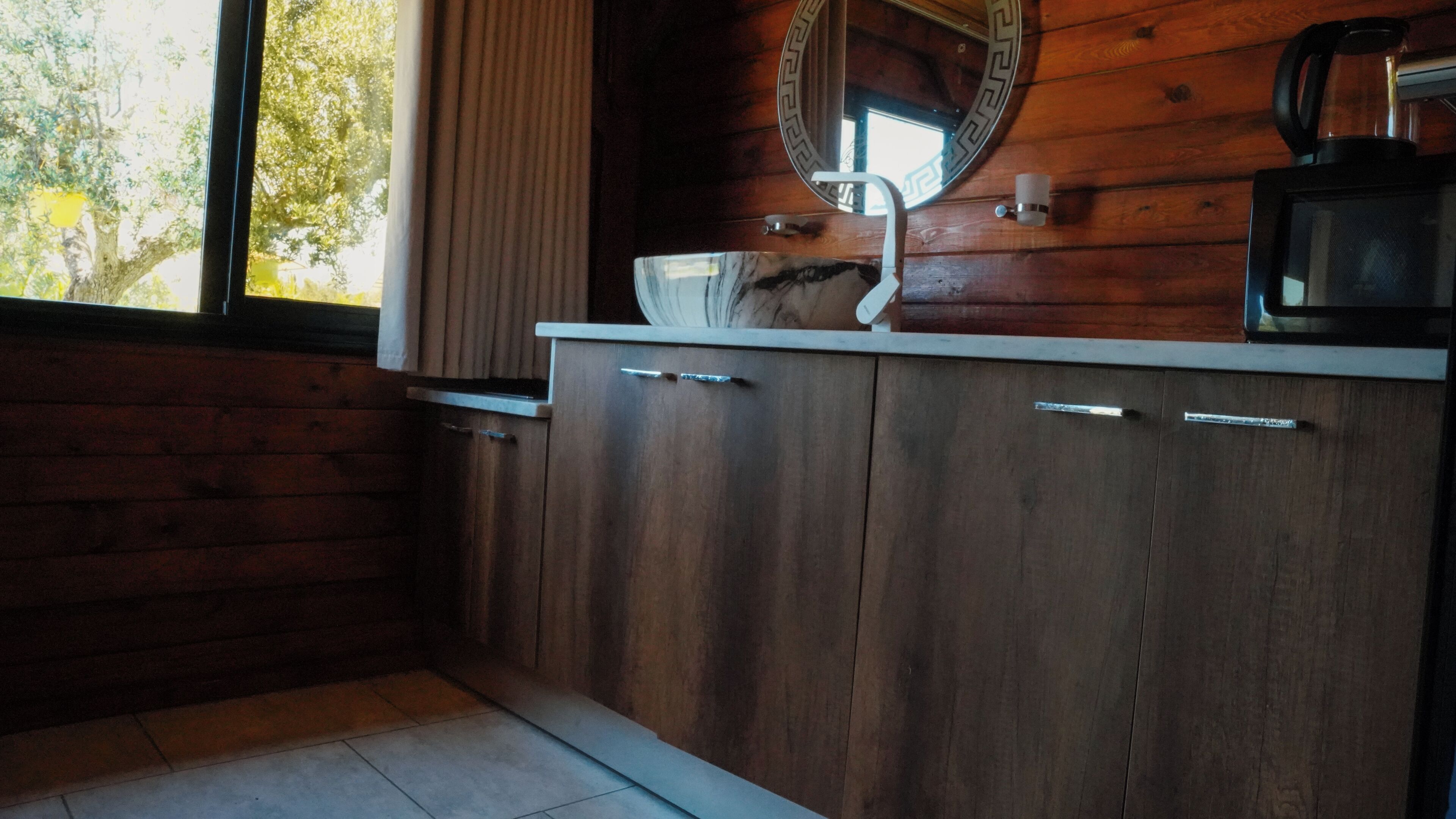 Interior de uma cabana de madeira com bancada branca, pia e cafeteira.