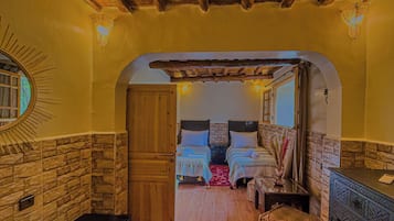 Quarto com parede de pedra, porta de madeira e cama com cabeceira.