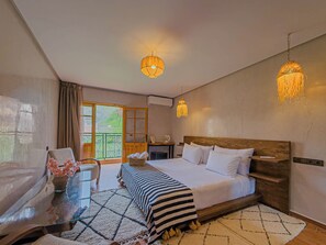 Quarto de hotel com cama, mesas de cabeceira, uma cadeira, janela com cortinas e duas luminárias suspensas.
