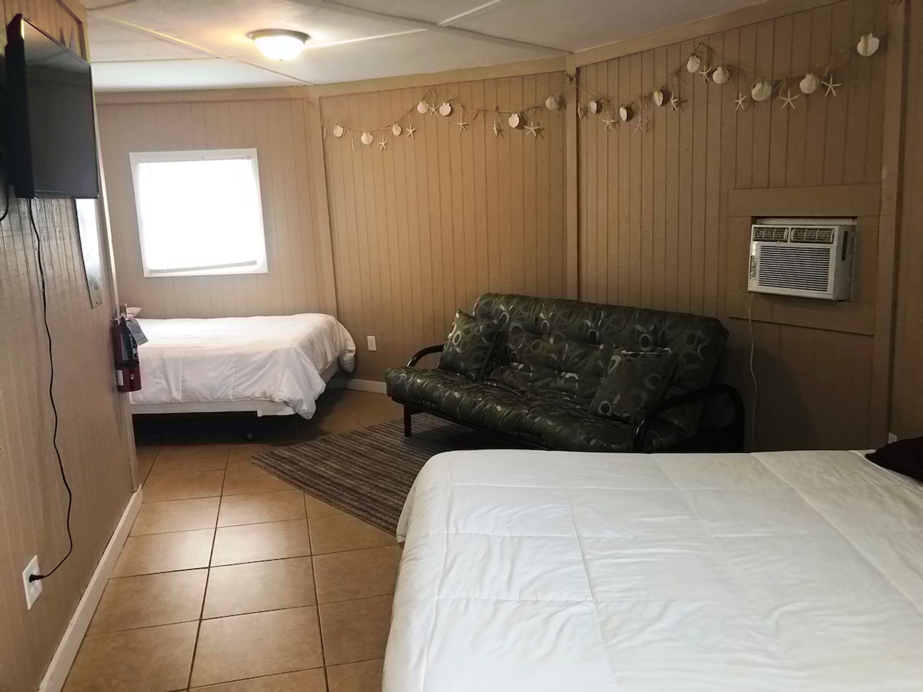 Quarto de hotel com duas camas, um sofá de couro, uma janela e ar-condicionado fixado na parede.