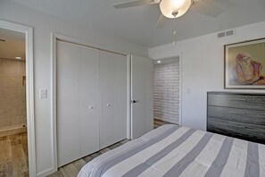 Quarto com cama, penteadeira, ventilador de teto e parede de tijolos.