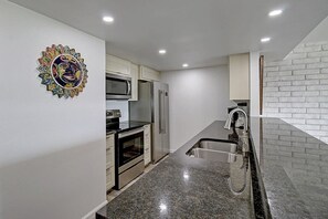 Uma cozinha moderna com eletrodomésticos de aço inoxidável, bancada de granito e um objeto decorativo na parede.