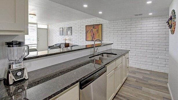 Uma cozinha moderna com bancada de granito, eletrodomésticos de aço inoxidável e painel de fundo de tijolos brancos.