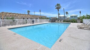 Piscina retangular com cerca branca e cadeiras de descanso de um lado.