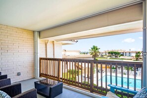 Varanda com móveis de vime, vista para uma piscina e um edifício ao fundo.