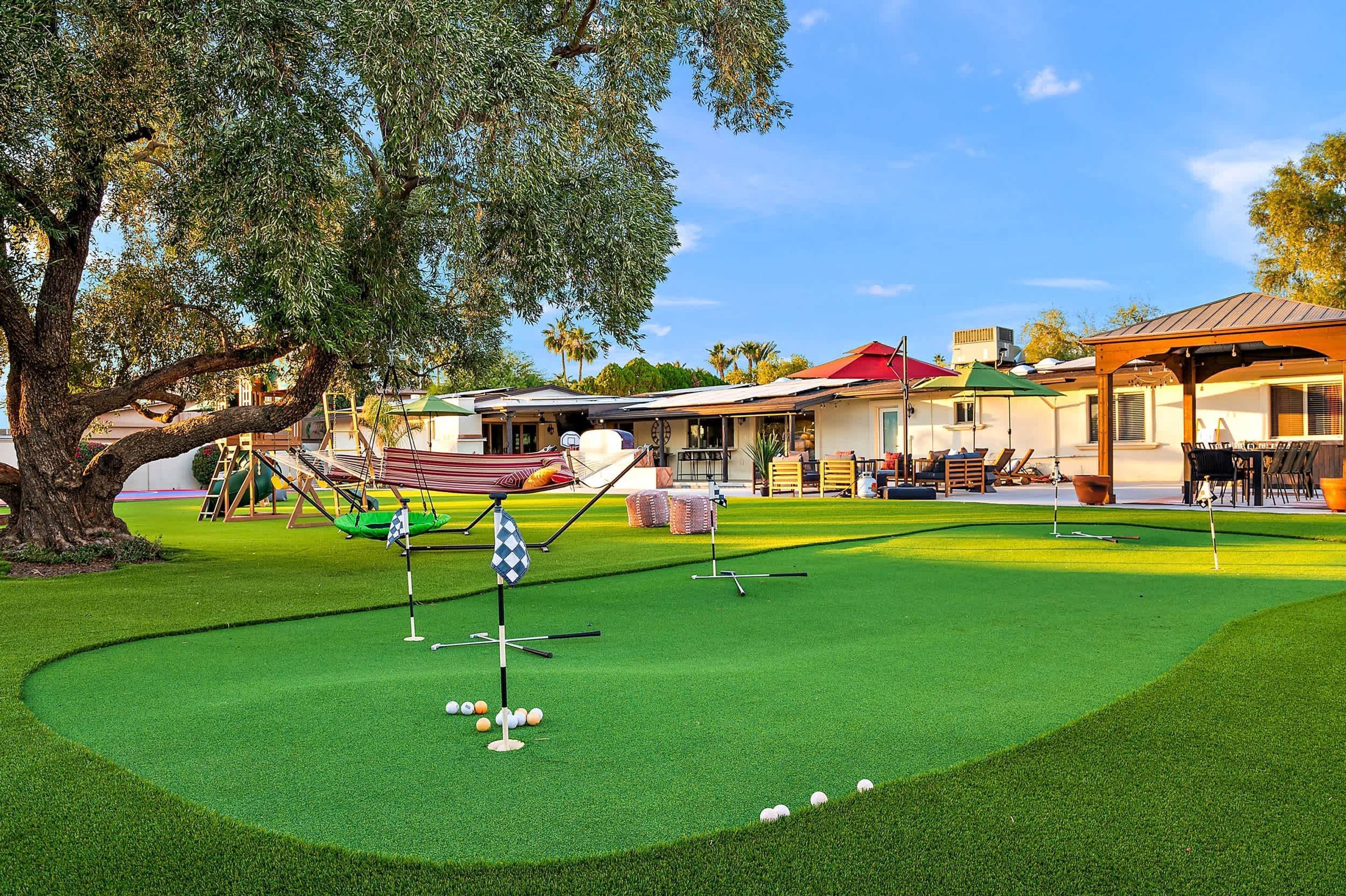 Um campo de golfe com putting green, uma rede para descanso e uma casa ao fundo.