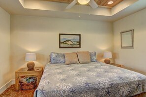 Quarto com cama, duas mesas de cabeceira, ventoinha no teto, quadro na parede e uma janela.