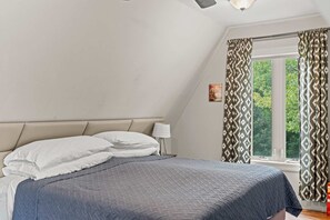 Quarto com cama, travesseiros, abajur e janela com cortinas.