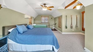 Quarto com uma cama grande, um ventilador de teto e uma janela com persianas.