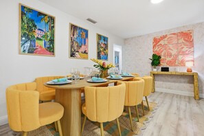 Uma sala de jantar com mesa redonda, cadeiras amarelas e obras de arte com tema tropical nas paredes.