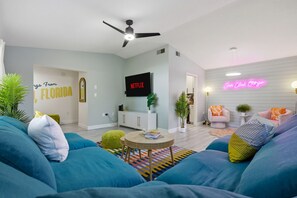 Uma sala de estar moderna com ventoinha no teto, TV de tela plana e um letreiro de neon.