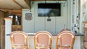 Uma área de bar com três cadeiras de vime, uma tela de televisão e um letreiro que diz 'Route 66'.