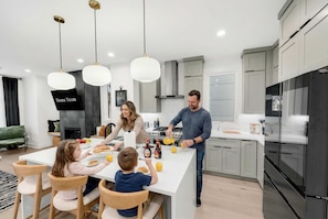 Uma cozinha moderna com ilha central, iluminação pendente e área de jantar com cadeiras.