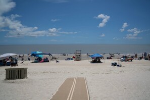 Uma praia com um calçadão de areia que leva à água, cadeiras de praia, guarda-sóis e uma torre de salva-vidas.