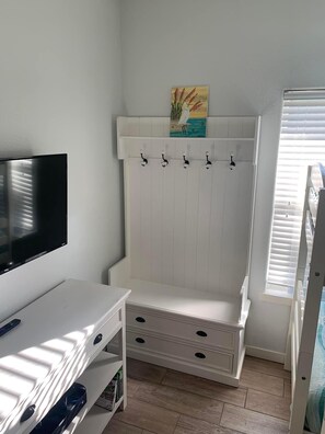 Quarto de criança com televisão, um armário branco, um cabideiro e um quadro na parede.