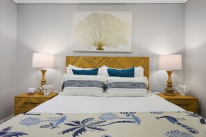 Cama bem arrumada com colcha estampada, com dois mesinhas de cabeceira com luminárias e objetos decorativos.