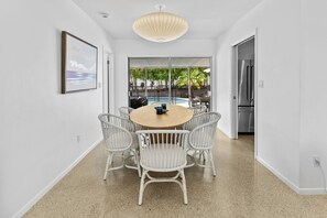 Cozinha moderna com armários brancos, geladeira de aço inoxidável e uma janela grande com vista para uma área de piscina.