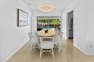Cozinha moderna com armários brancos, geladeira de aço inoxidável e uma janela grande com vista para uma área de piscina.
