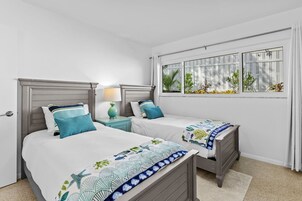 Quarto com duas camas, mesa de cabeceira, abajur e janela com vista para plantas.