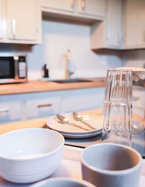 Uma cozinha moderna com uma mesa de jantar posta para dois, com um jarro de vidro transparente, pratos, tigelas e talheres.