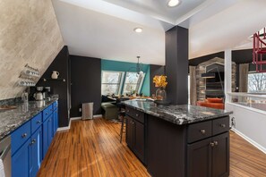 Cozinha moderna com armários escuros, bancada de mármore e piso de madeira.