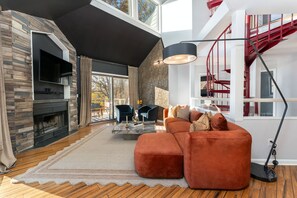 Uma sala de estar moderna com lareira de pedra, um amplo sofá modular e uma escada vermelha.