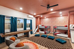 Quarto compacto com beliches, mesa de pebolim e janela com cortinas.