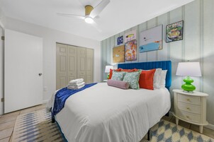 Quarto de hotel com cama, mesa de cabeceira, ventilador de teto e obras de arte na parede.