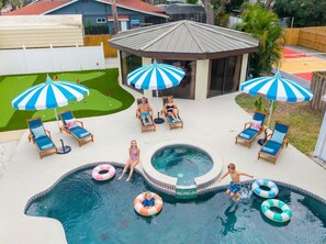 Área de piscina com espreguiçadeiras e guarda-sóis, cercada por um jardim.