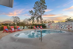 Uma área de piscina com espreguiçadeiras e guarda-sóis, cercada por árvores e um muro decorativo.