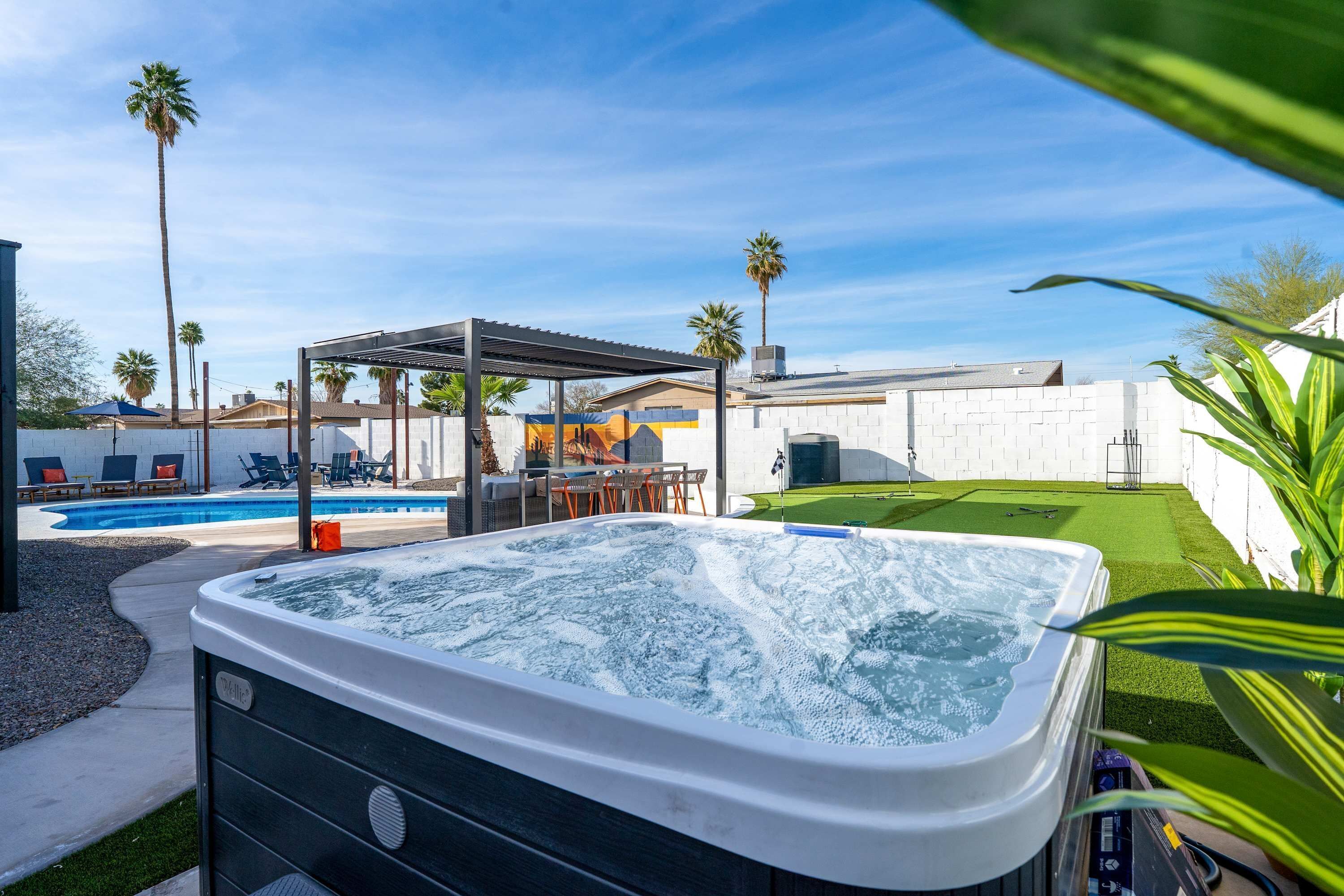 Uma banheira de hidromassagem com pérgola, uma piscina e palmeiras.