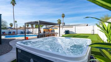 Uma banheira de hidromassagem com pérgola, uma piscina e palmeiras.