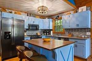 Uma cozinha moderna com armários azuis, uma ilha central, eletrodomésticos de aço inoxidável e uma luminária decorativa no teto.
