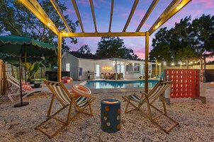 Uma área à beira da piscina com espreguiçadeiras, piscina e um alpendre coberto.