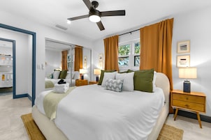 Quarto moderno com uma cama grande, duas mesas de cabeceira, um ventilador de teto e vista para o exterior pela janela.