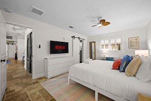 Quarto com cama, televisão na parede, ventoinha no teto e janela com persianas.