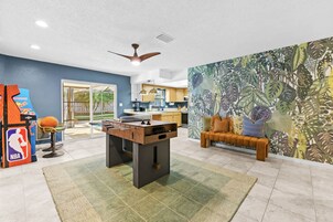 Uma sala de estar ampla com mesa de pebolim, um banco e parede com mural tropical.