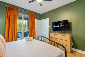 Um quarto com uma cama, televisão, penteadeira e janela com cortinas.